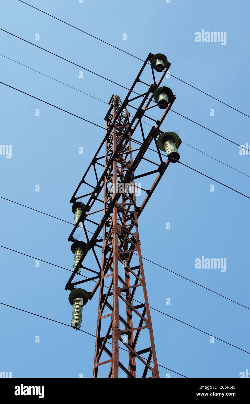 Electricity pylon with insulators and power lines. Blue sky background. Rusty weathered metal ...