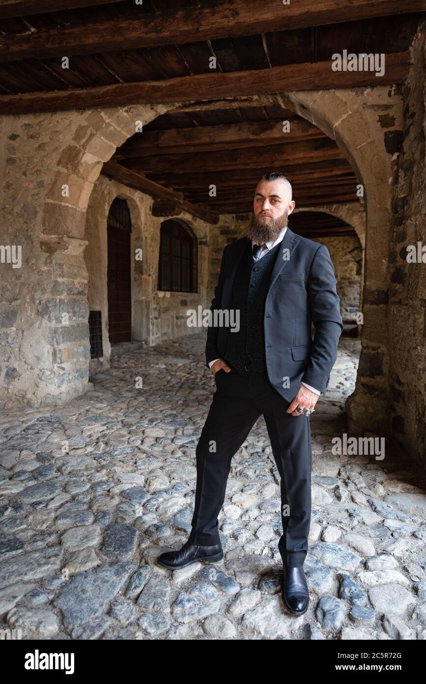 Man in dark elegant suit posing under the arcades of a medieval Italian ...