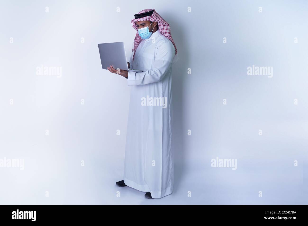 Saudi Arab Man standing and using laptop while wearing face mask Stock ...