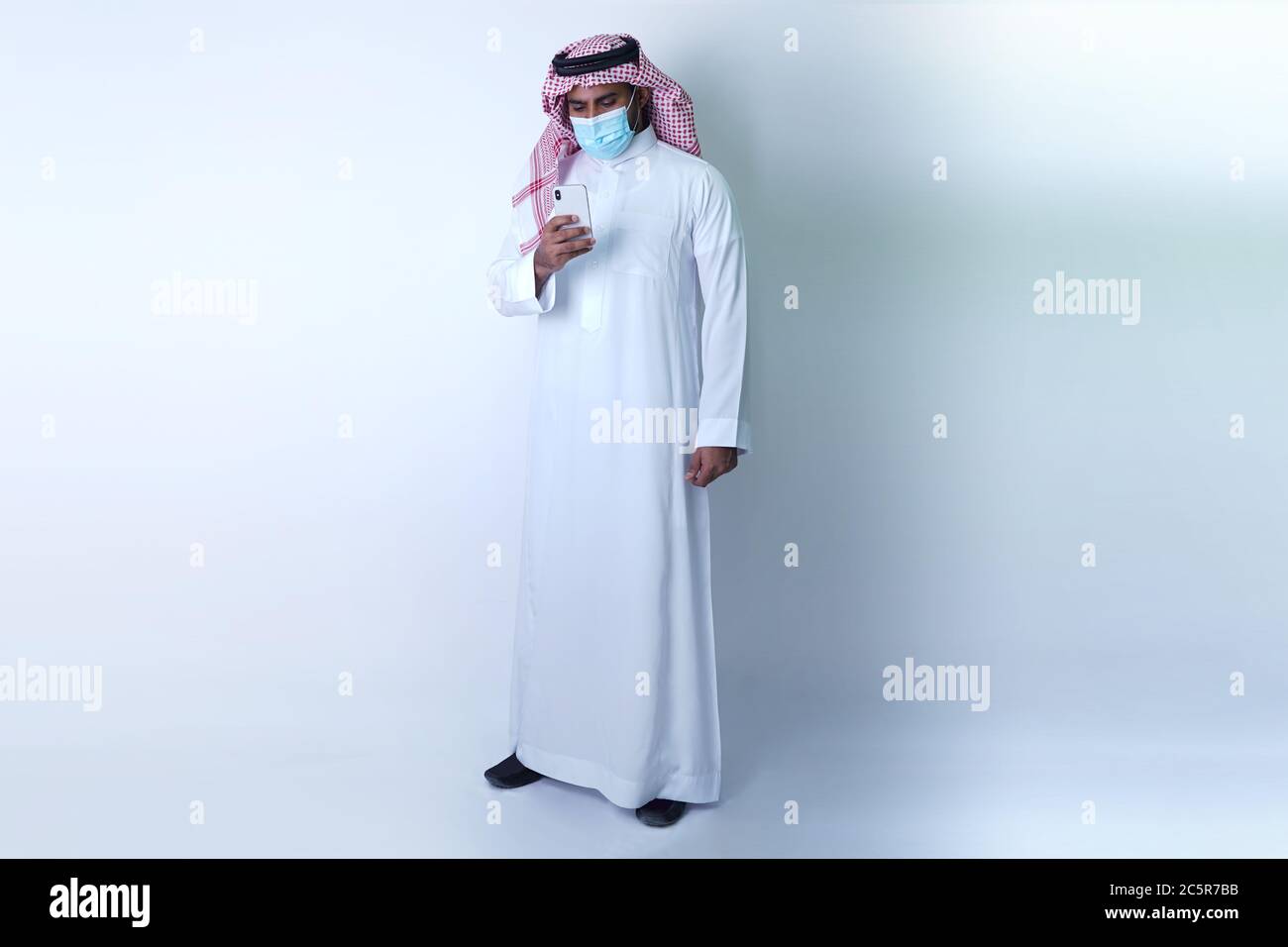 Saudi Arab Man standing and using mobile phone while wearing face mask ...