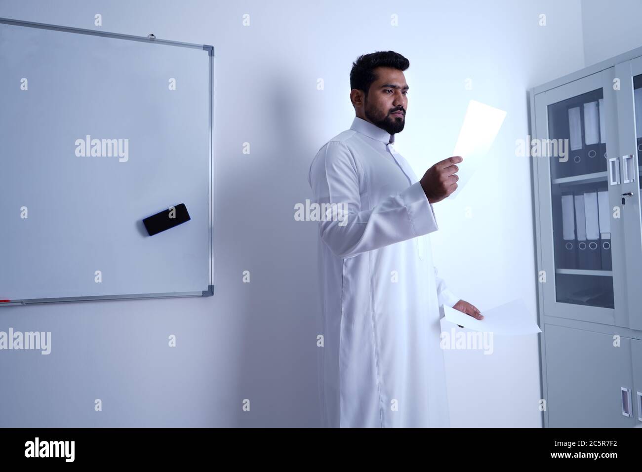 Saudi Arab Man standing in office and reading paper and analysing ...