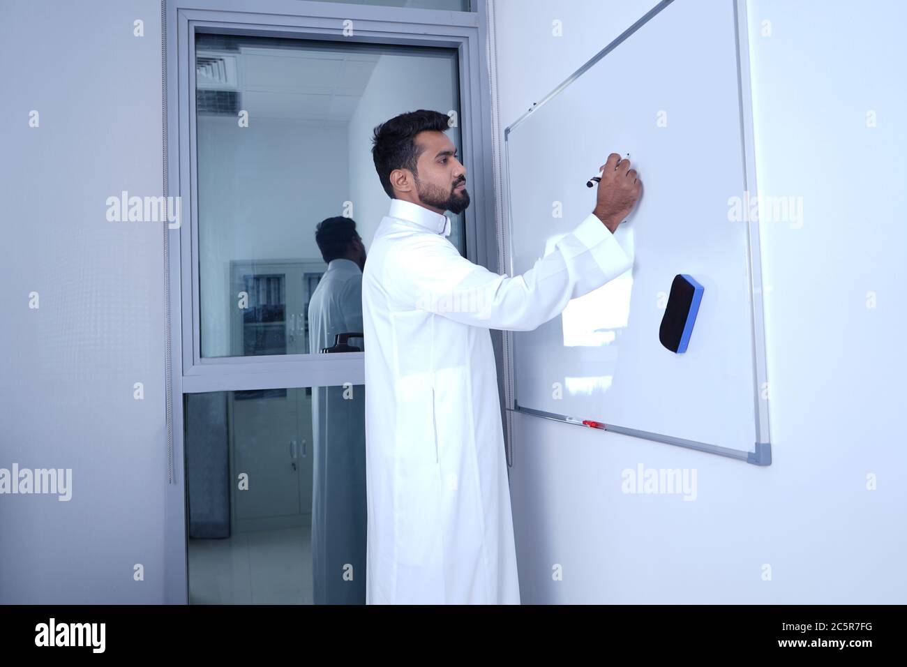 Saudi Arab Man standing in office while writing on white board with ...