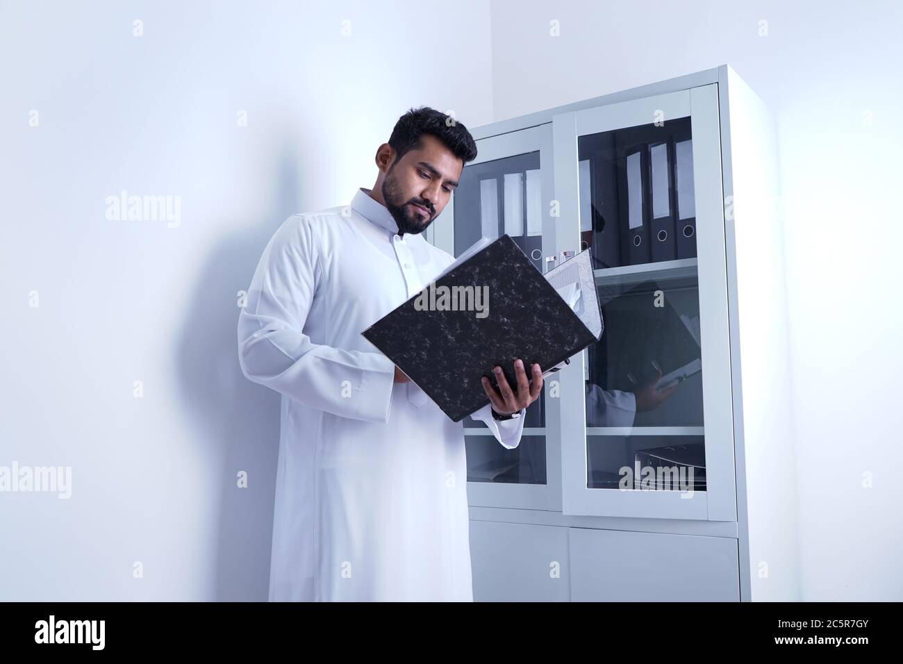 Saudi Arab Man standing in office and reading file Stock Photo - Alamy