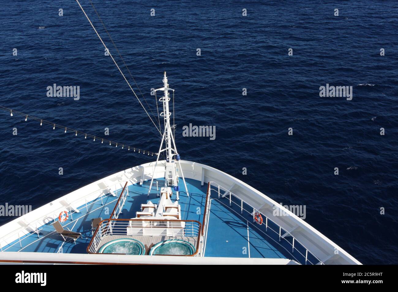 Bow of cruise ship cruising through deep blue ocean with white and blue ...
