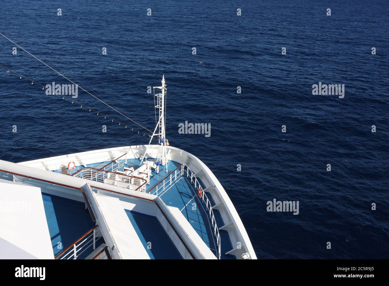 Bow of cruise ship cruising through deep blue ocean with white and blue ...