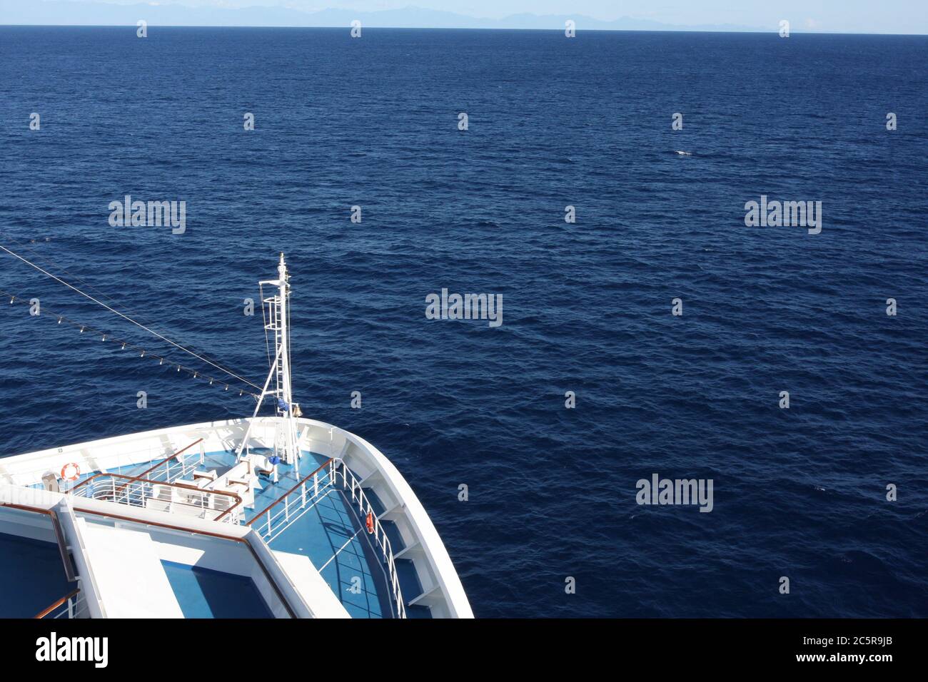 Bow of cruise ship cruising through deep blue ocean with white and blue ...