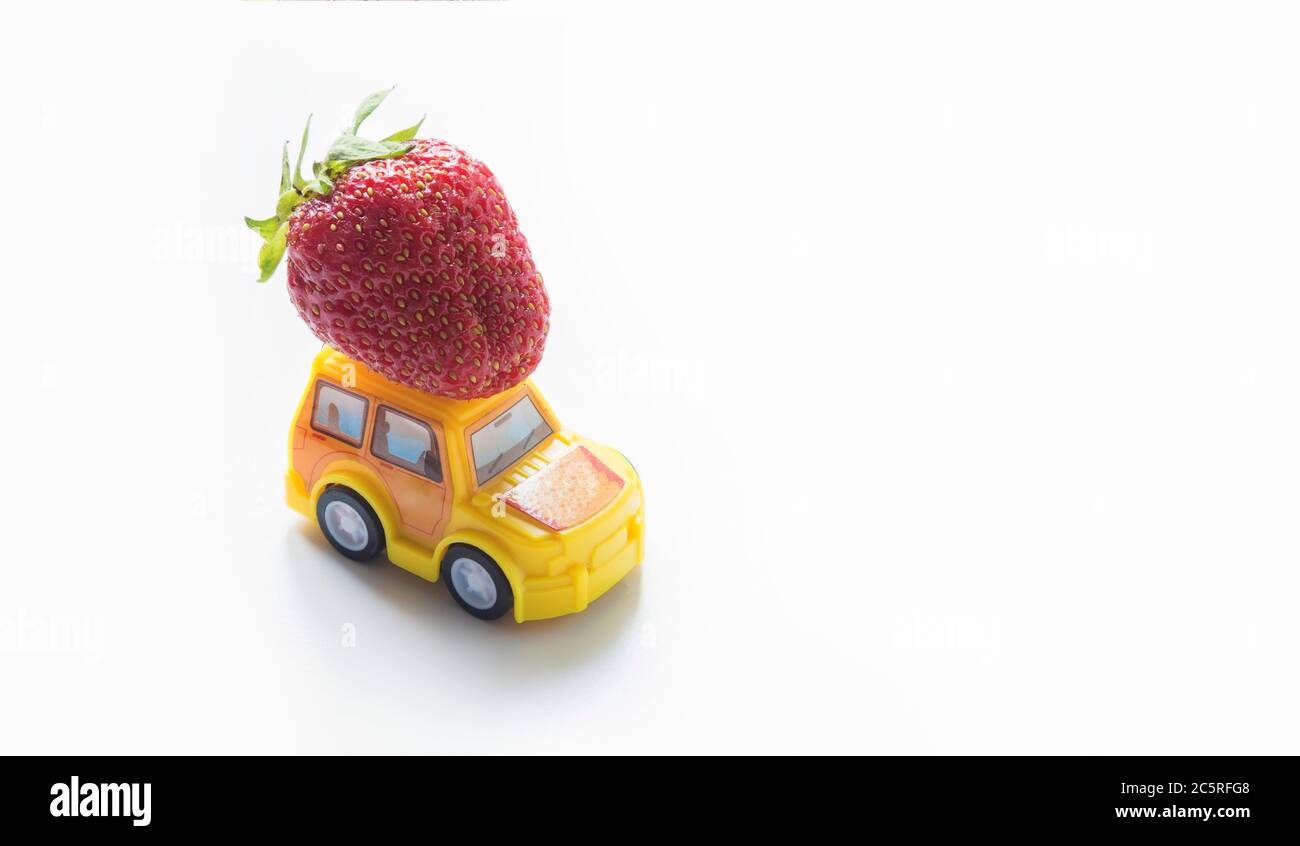 A small children's toy car carries a fresh garden strawberry on a white ...