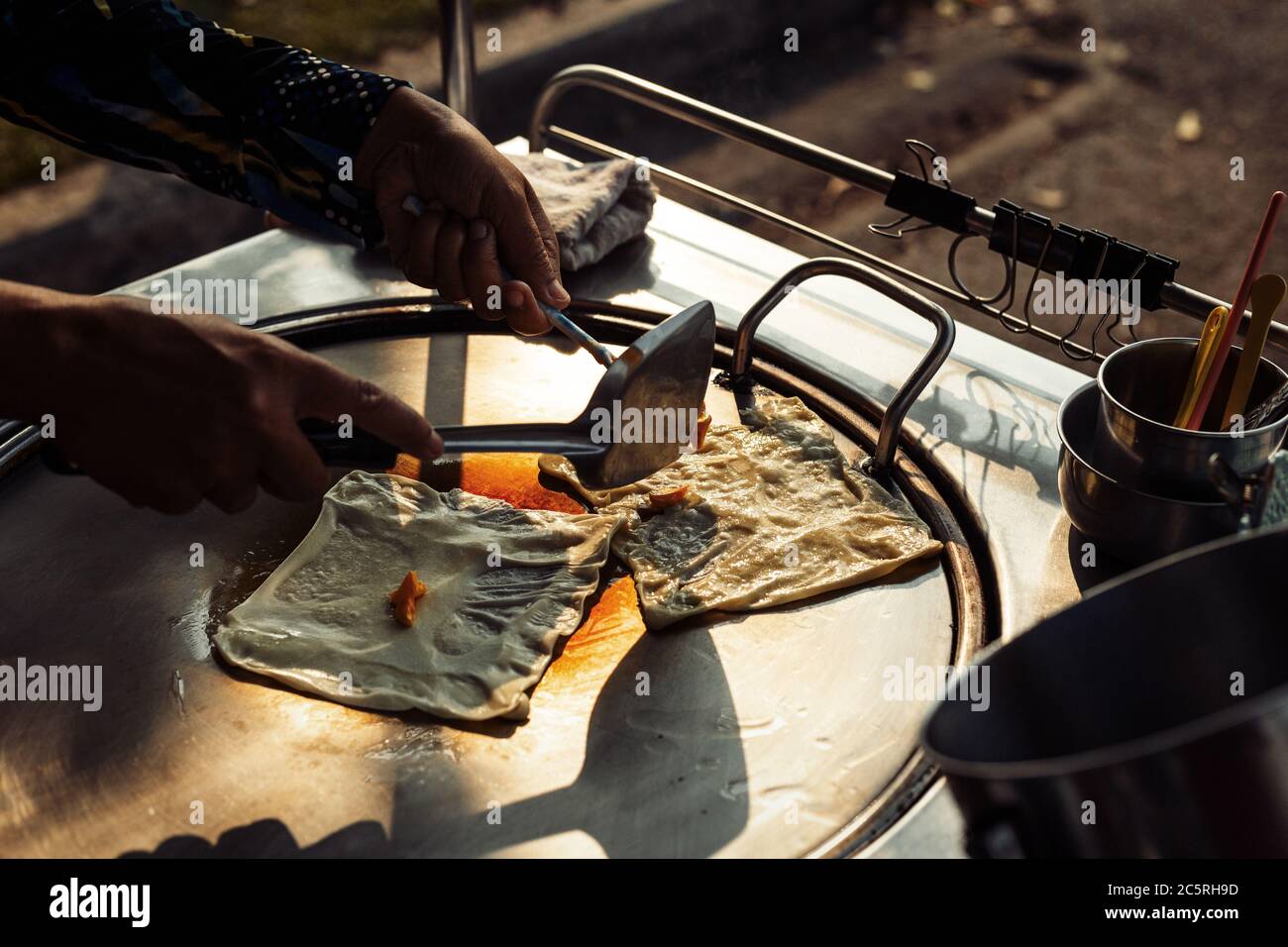 Hands of street vendor cooking Thai style sweet roti bread on steel ...