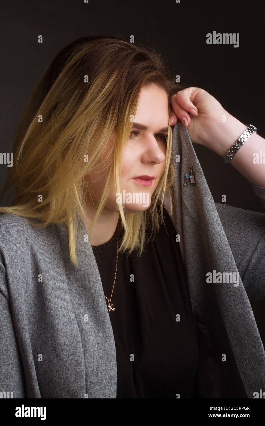 blonde Plus Size Model on a black background in a grey jacket hiding ...