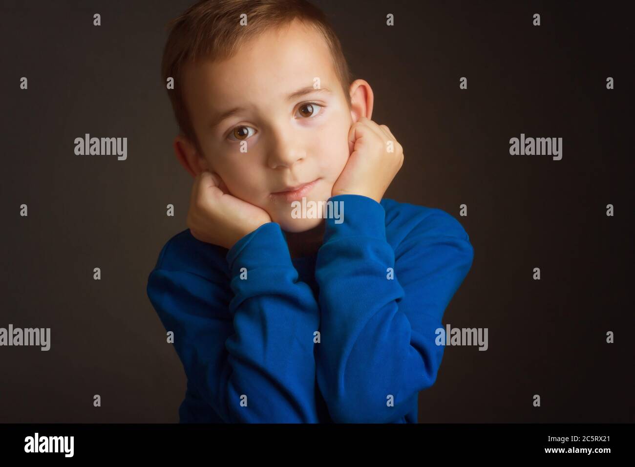 Studio portrait of boy in a blue classic sweater on a dark background ...