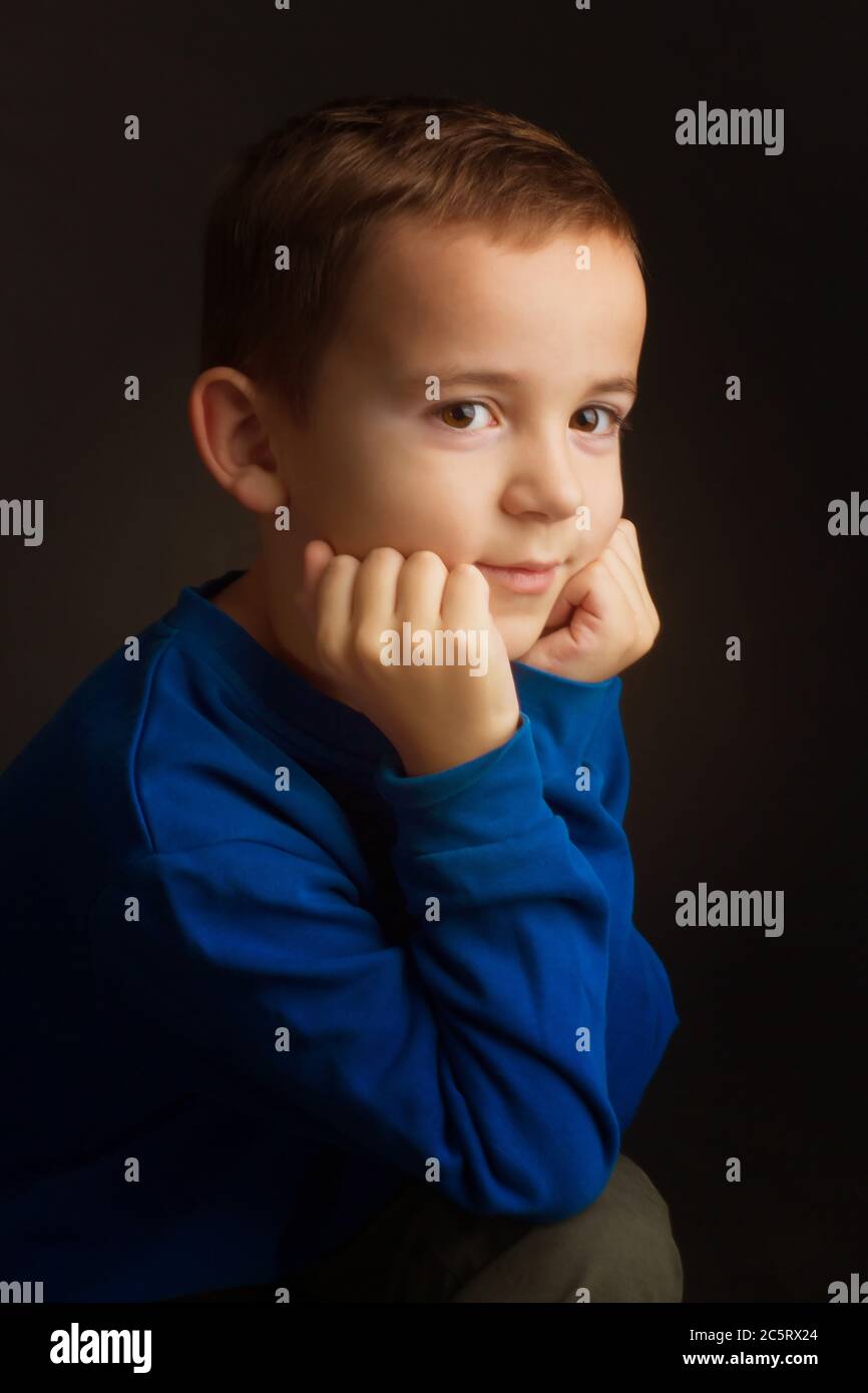 Studio portrait of boy in a blue classic sweater on a dark background ...