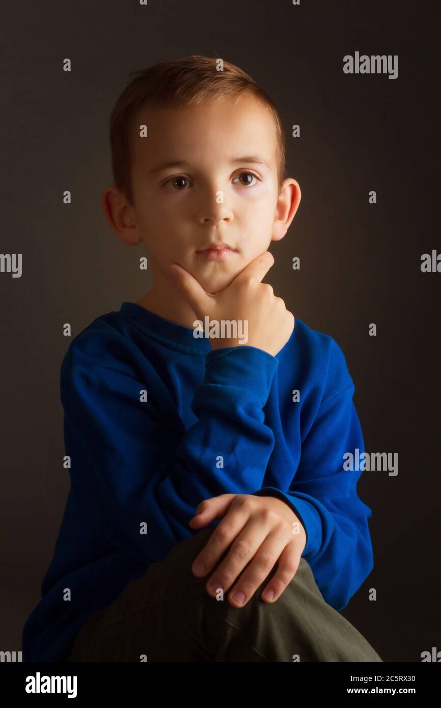 Studio portrait of a boy in a blue classic sweater, sitting on a chair ...