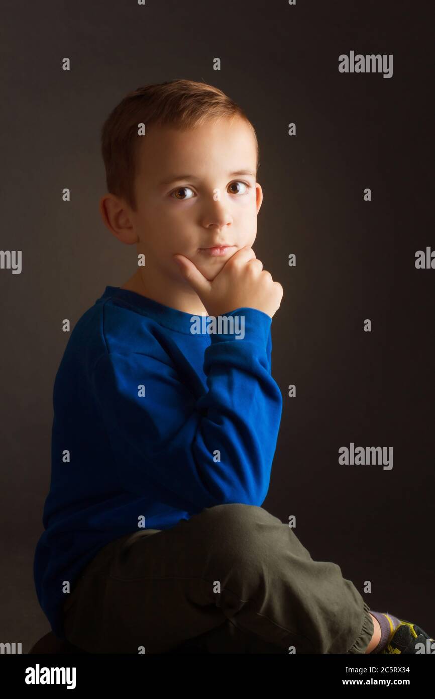 Studio portrait of a boy in a blue classic sweater, sitting on a chair ...