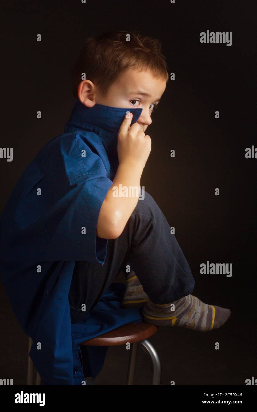 Studio portrait of a boy in a blue classic sweater, sitting on a chair ...