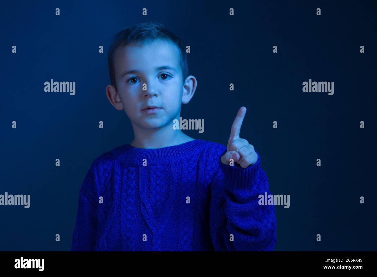 Studio portrait of a brunette Boy who counts on his fingers, shows one ...