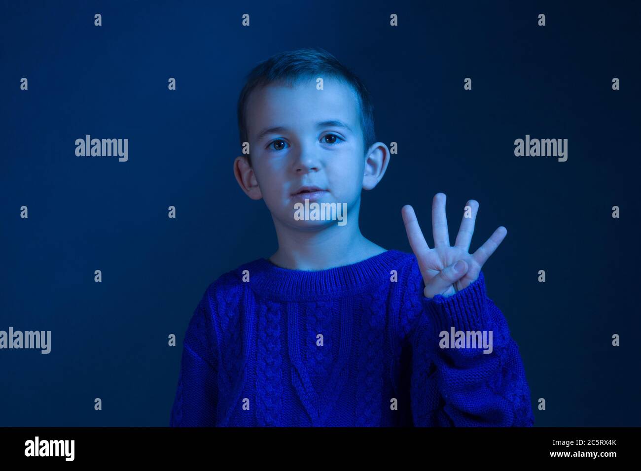 Studio portrait of a brunette Boy who counts on his fingers, shows four ...