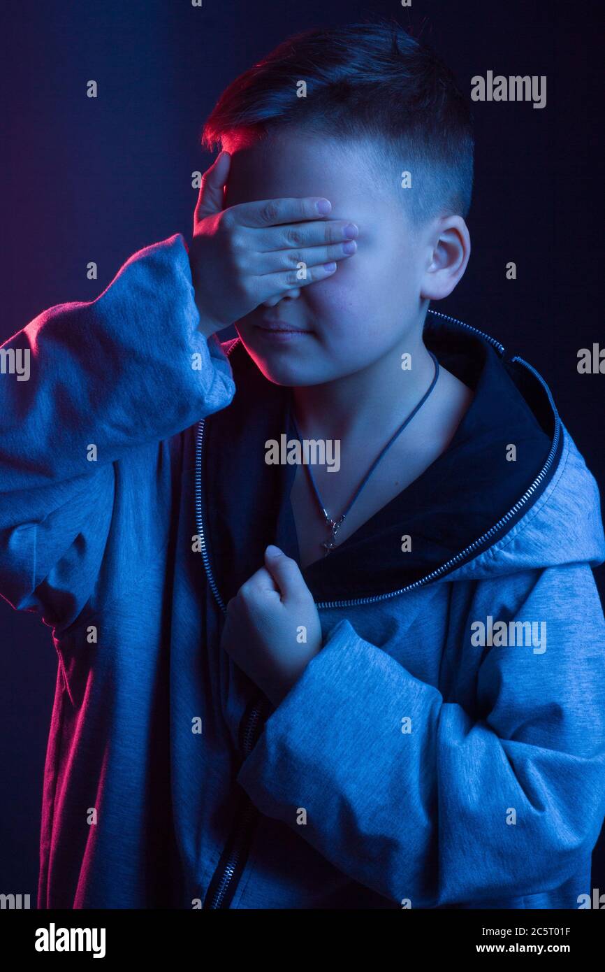 Studio portrait of a dark-haired boy, on a dark background, in a hoodie ...