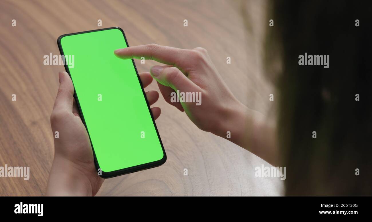 Young woman sitting at a table and using a smartphone with vertical green screen Stock Photo - Alamy