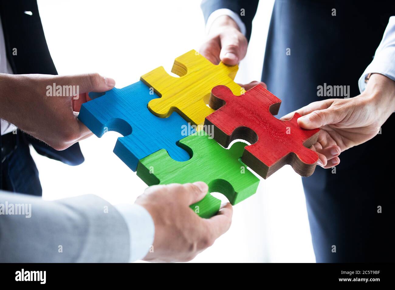 Business people team assembling four color jigsaw puzzle pieces unity ...