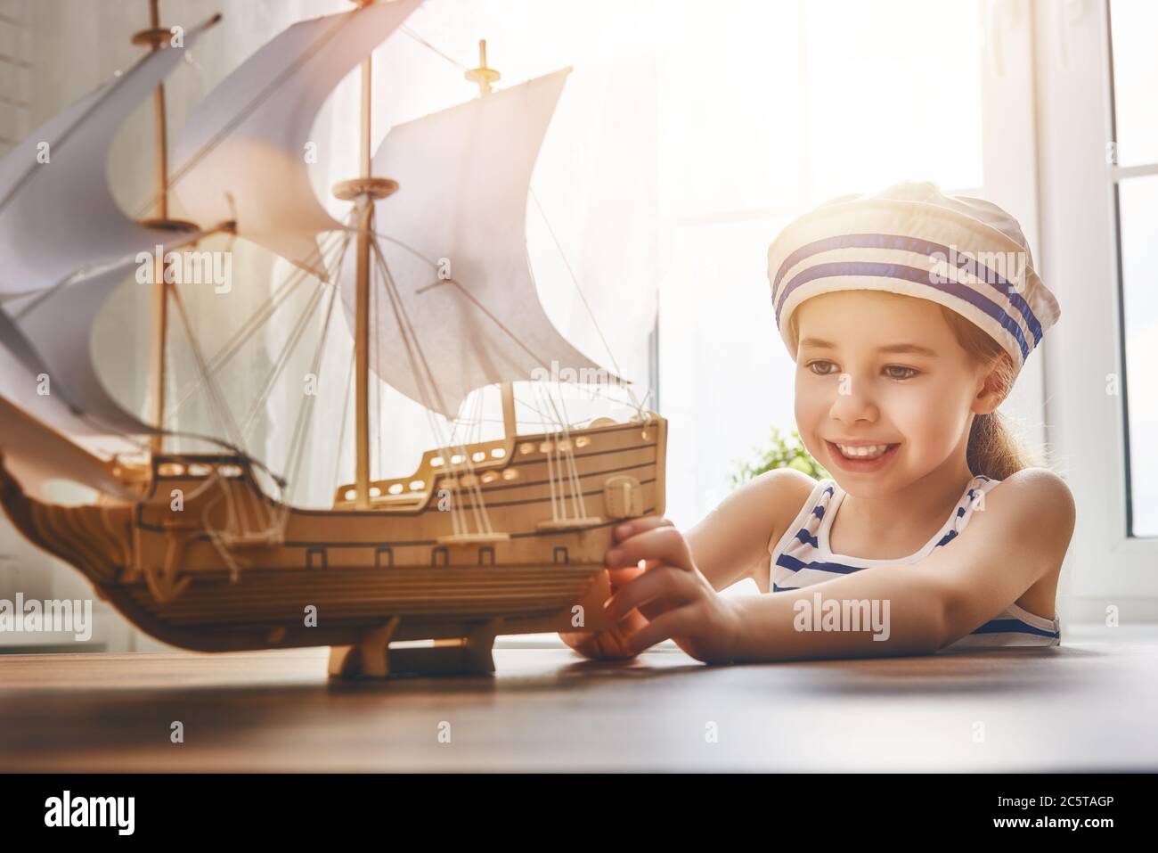 Adorable little child girl looks at toy ship and dreams of sea ...
