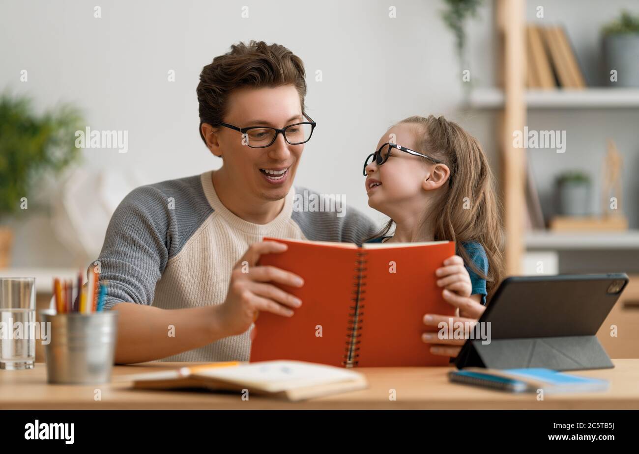 Back to school. Happy child and adult are sitting at desk. Girl doing ...