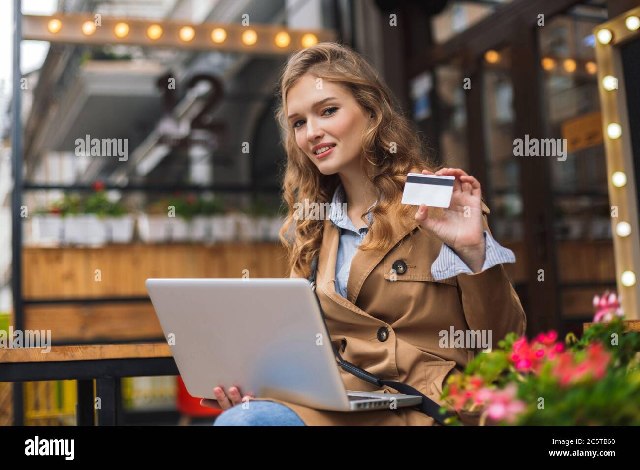 Pretty smiling woman in trench coat dreamily looking in camera while ...