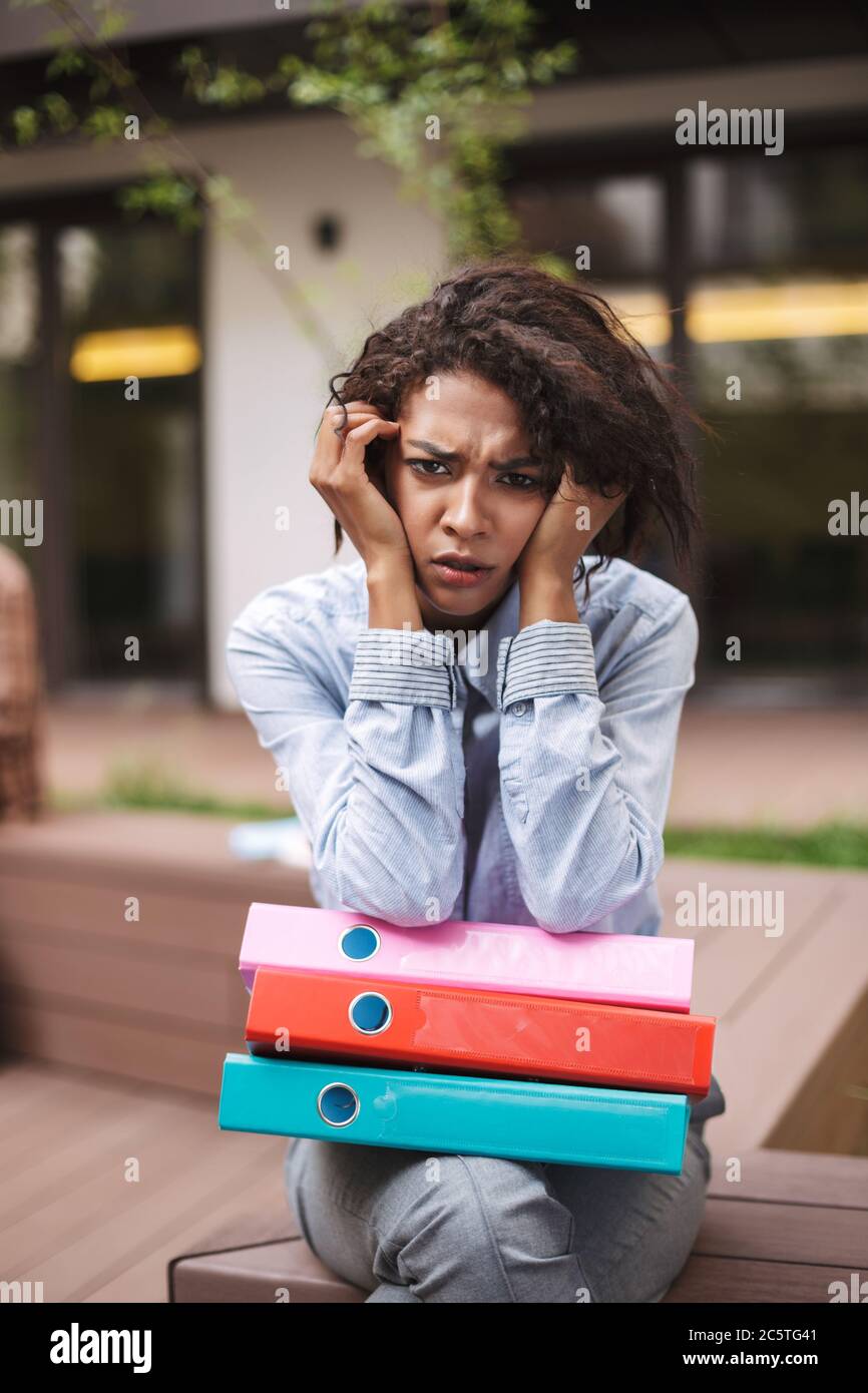 Portrait of upset lady sitting on bench with colorful folders and sadly ...