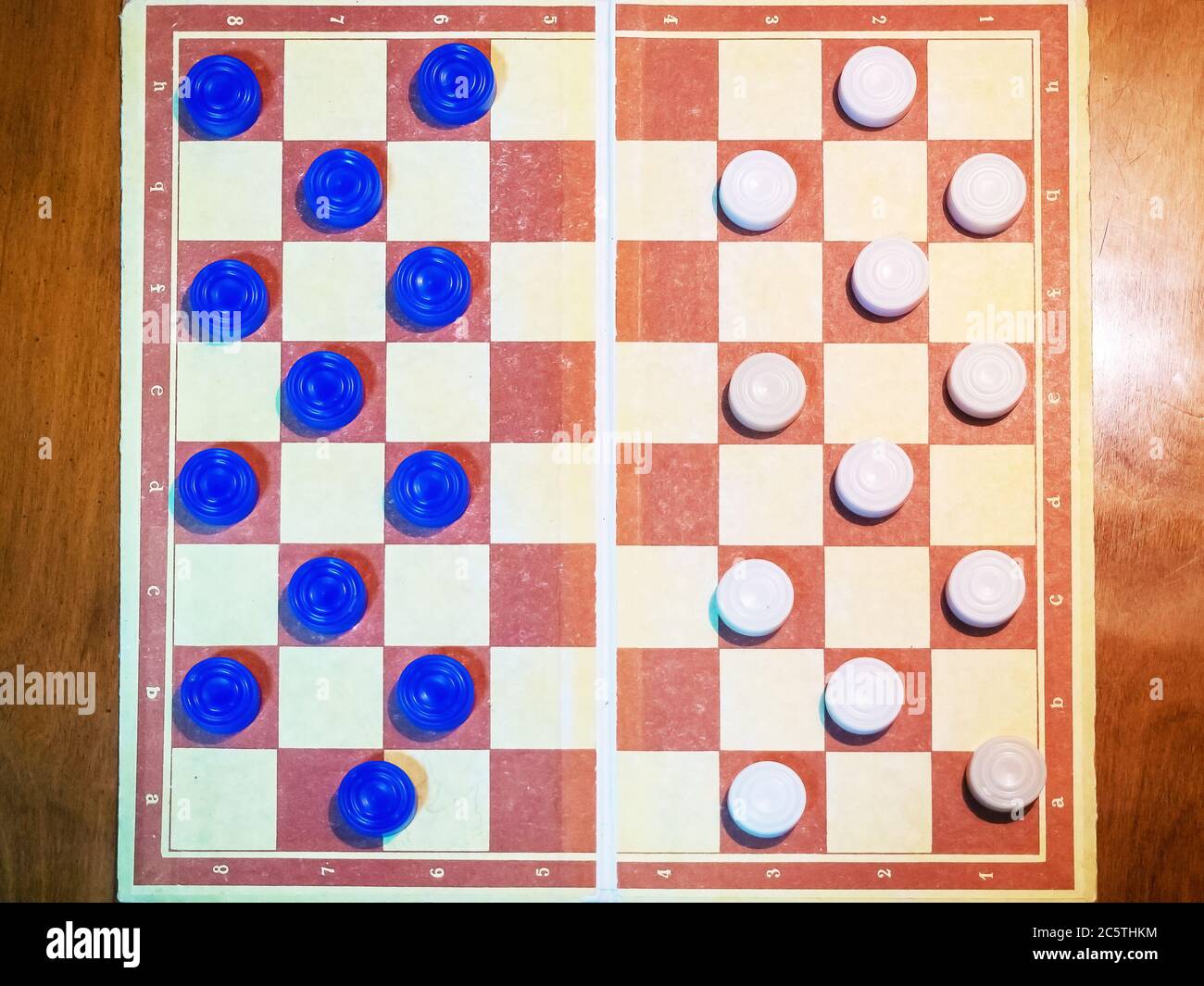 Old checkered board with plastic checkers on a wooden table. A game of ...