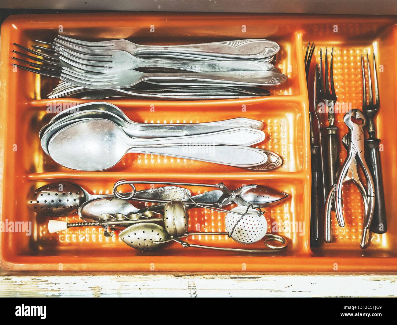 Closeup photo of an orange plastic cutlery container with old spoons ...