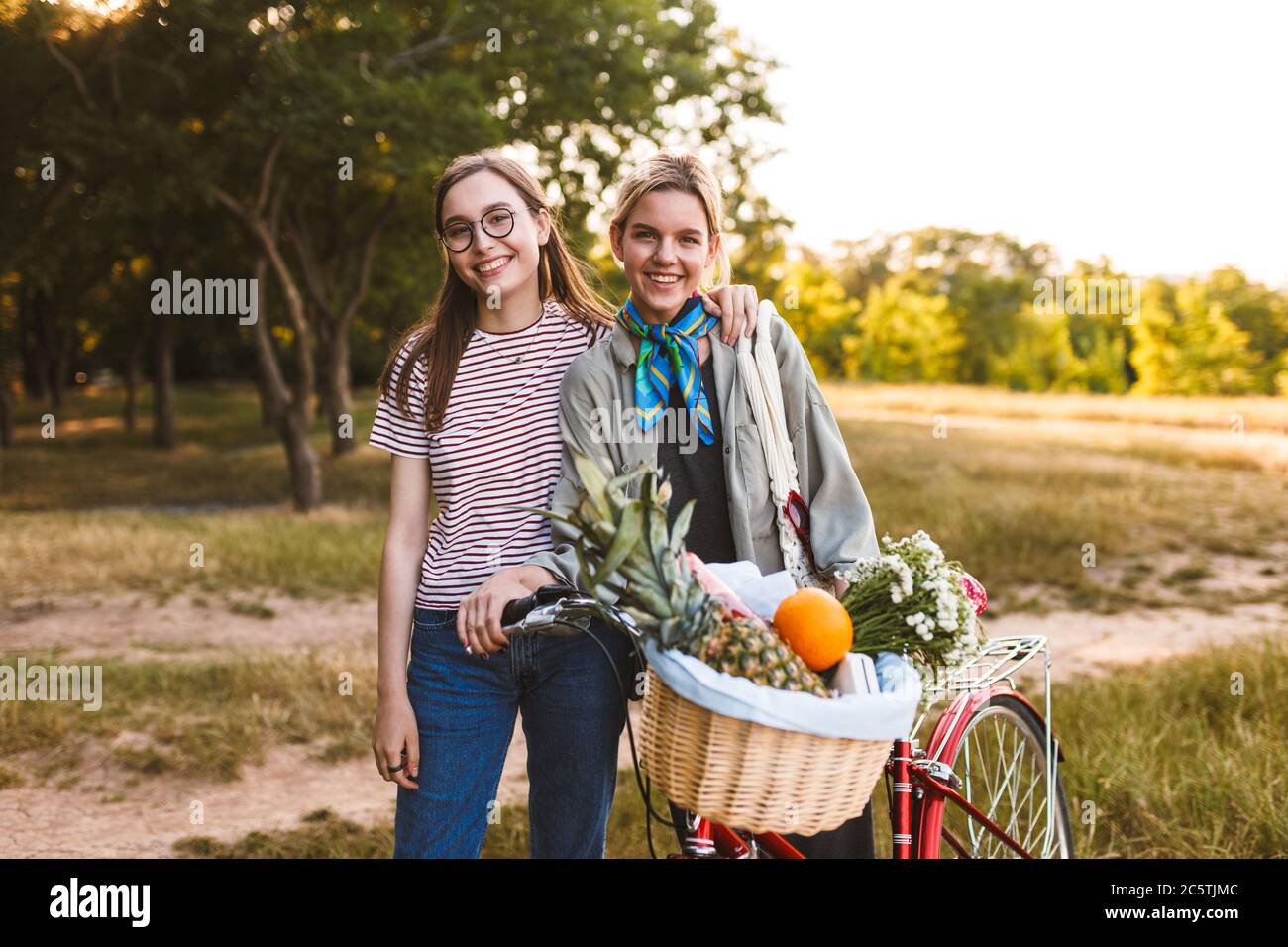 Two pretty smiling girls with bicycle and basket full of wildflo Stock ...