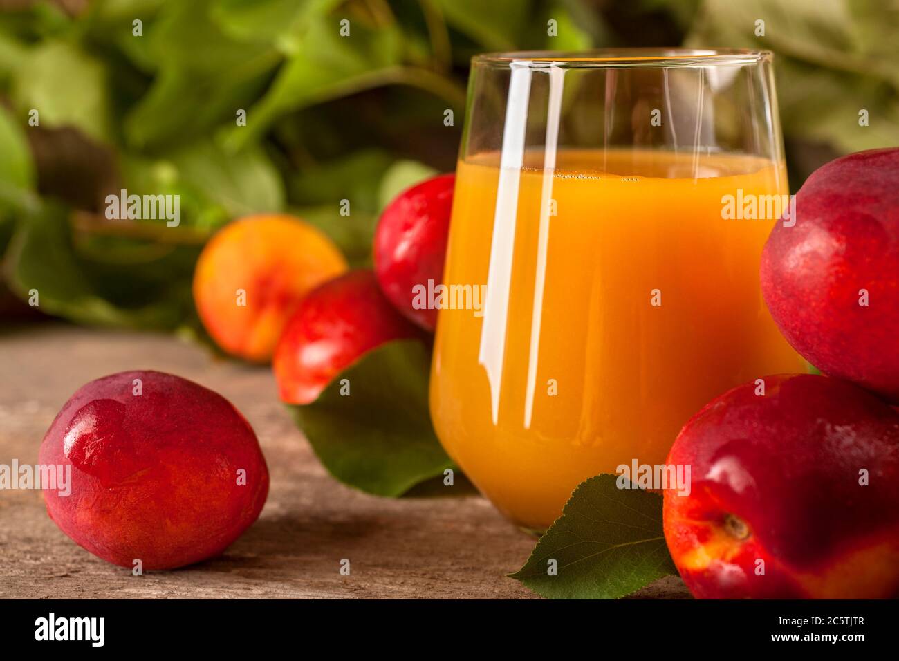 A glass of nectarine juice with fresh nectarines on rustic background ...