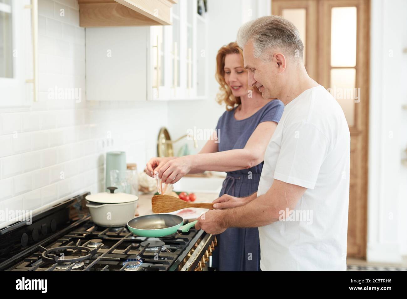 Waist up portrait of cheerful mature couple cooking breakfast together ...