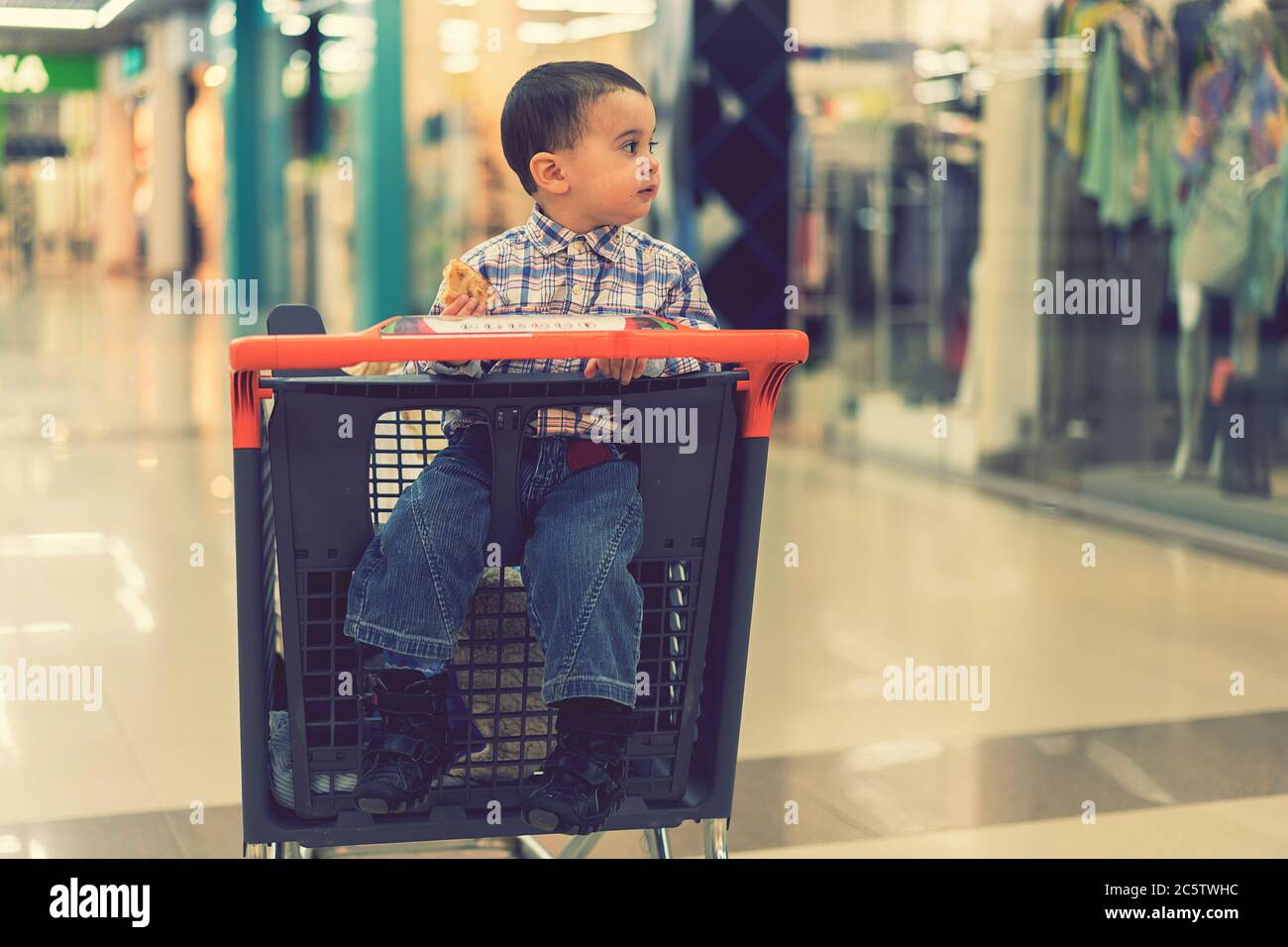 Baby boy rides in a trolley through a shopping center. toned Stock ...