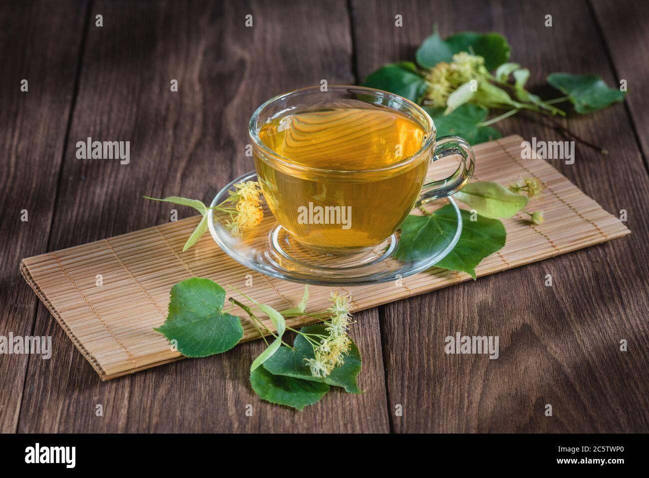 A cup with fragrant lime tea, standing on a wooden table, in the rays ...