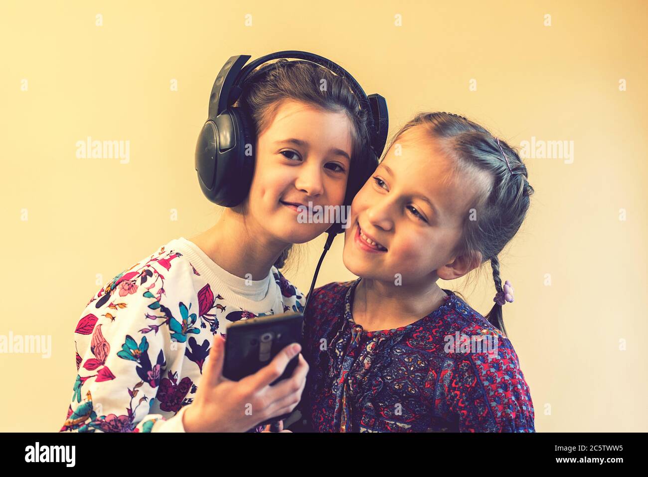 Two little girls together listen to music. toned Stock Photo - Alamy