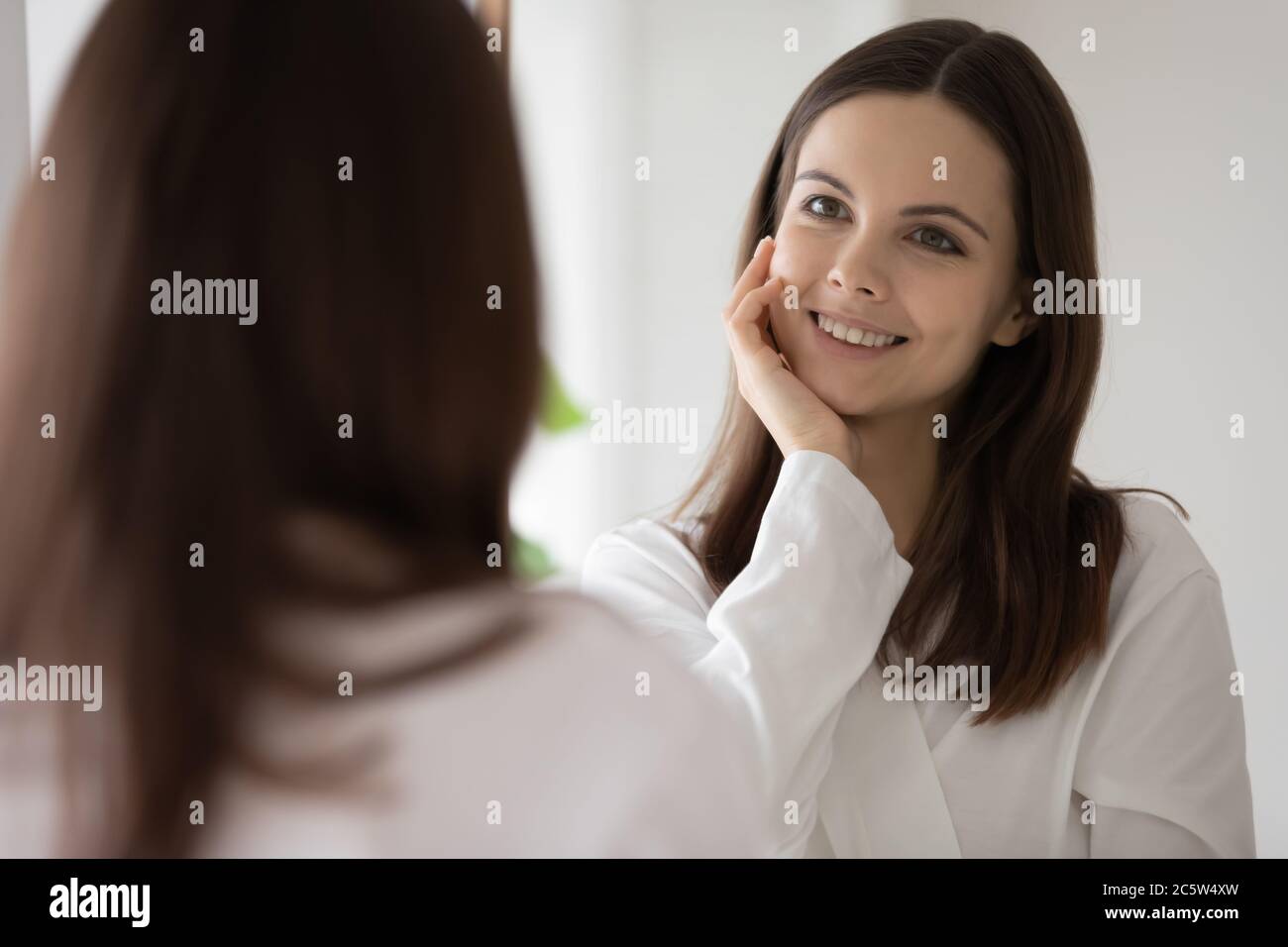 Smiling beautiful young woman looking at mirror in bathroom Stock Photo ...