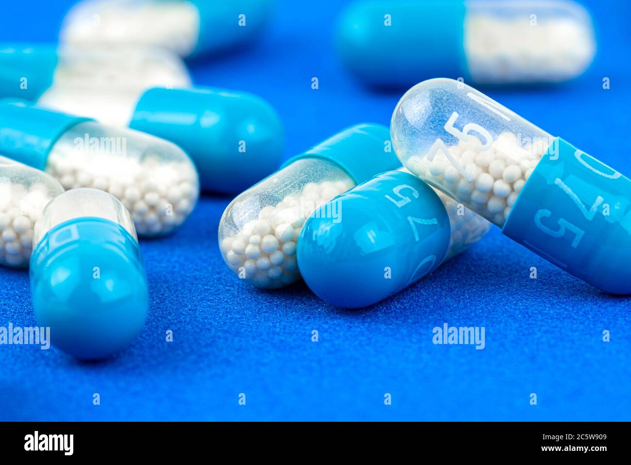 Blue gelatin capsules with white granules inside, isolated on a blue ...