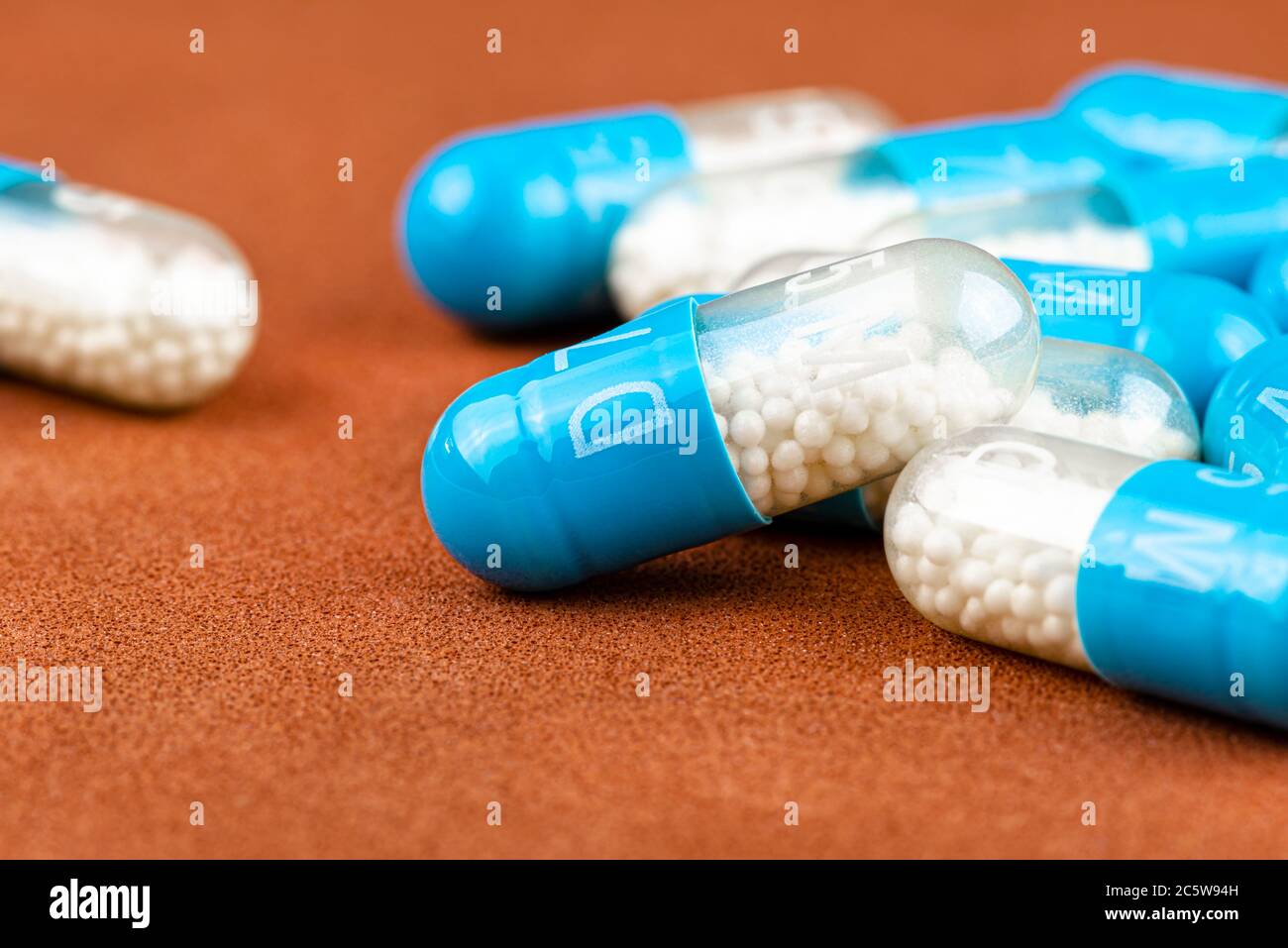 Blue gelatin capsules with white granules inside, isolated on a brown ...