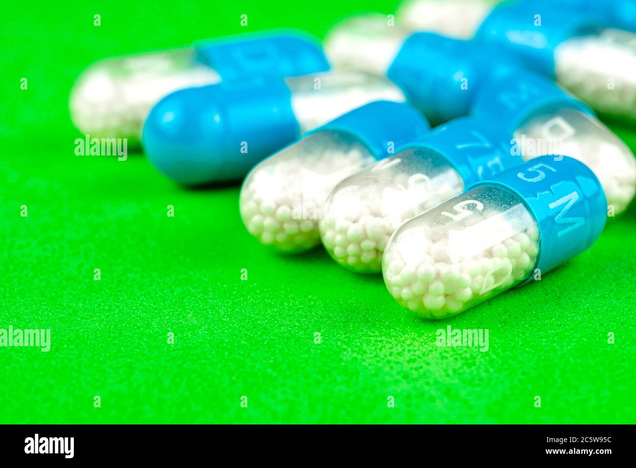 Blue gelatin capsules with white granules inside, isolated on a green ...