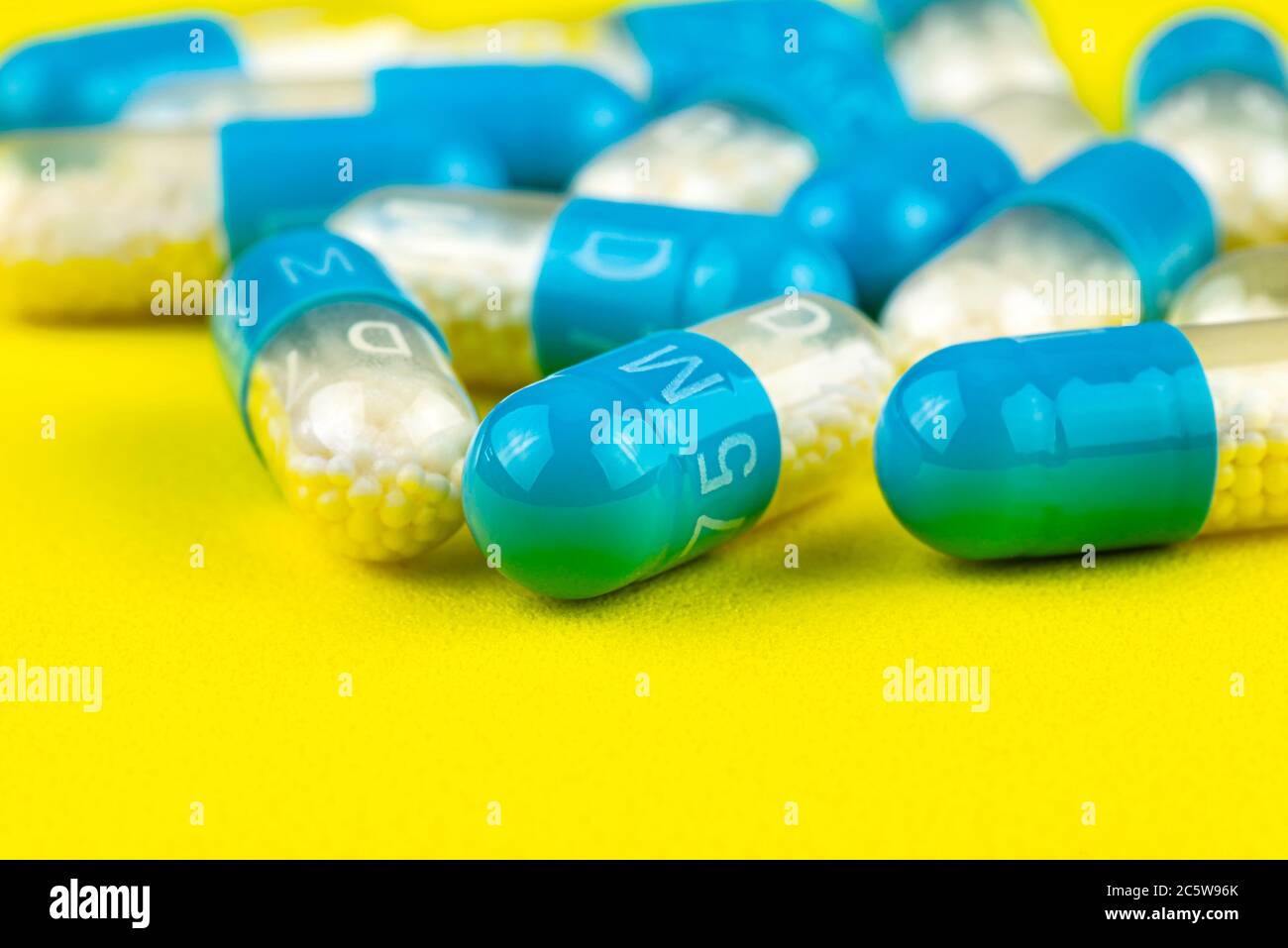 Blue gelatin capsules with white granules inside, isolated on a yellow ...