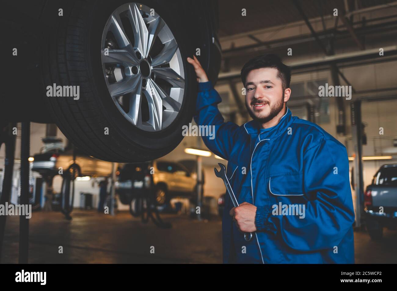 Auto mechanic with wrench stands near a car on a lift. Car repairman in ...