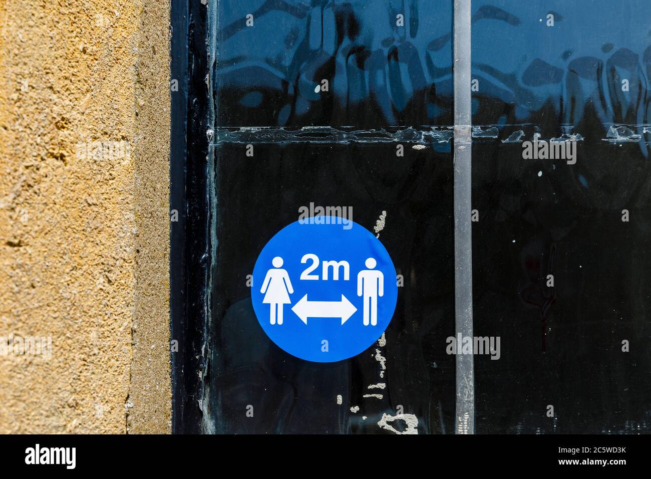 Blue sign taped on a wall outside a shop reminding compliance with 2m ...