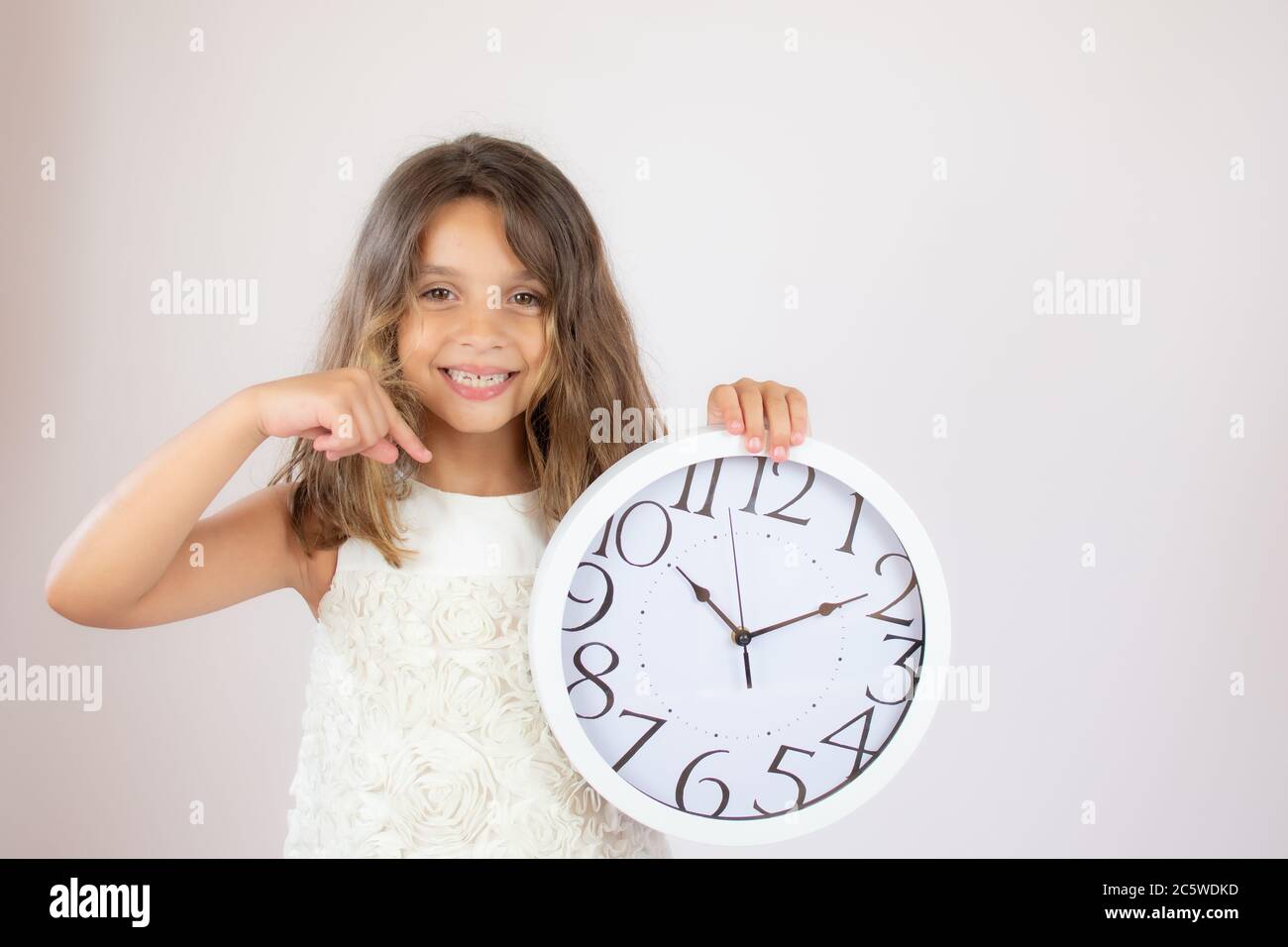 Beautiful girl smiling showing a clock Stock Photo - Alamy