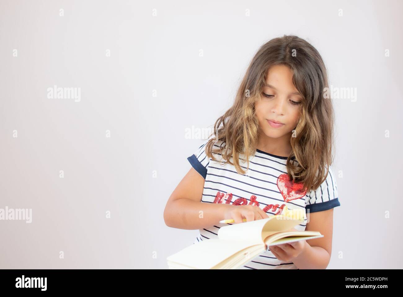 Pretty little girl in striped shirt writing in a notebook Stock Photo ...