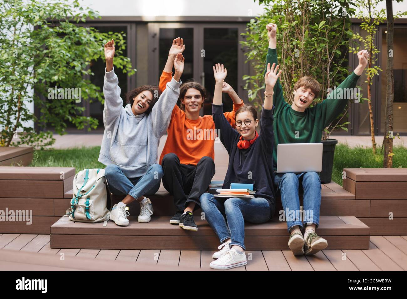 Group of joyful students sitting and happily looking in camera while ...