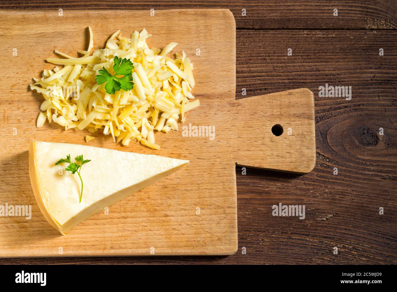 Grated cheese and cheese triangle with parsley on cutting board on ...