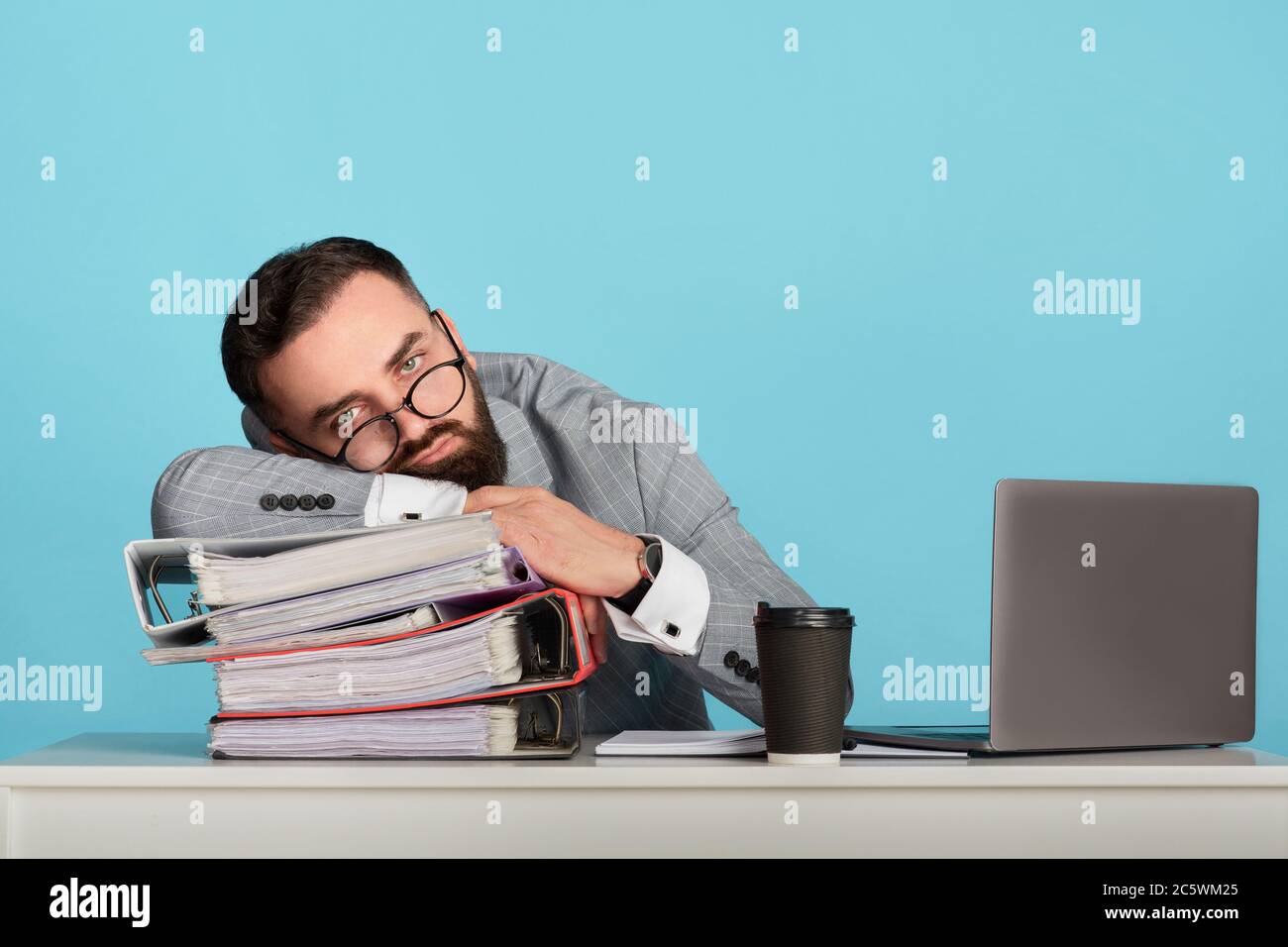 Overworked businessman lying on desk near laptop computer against blue ...