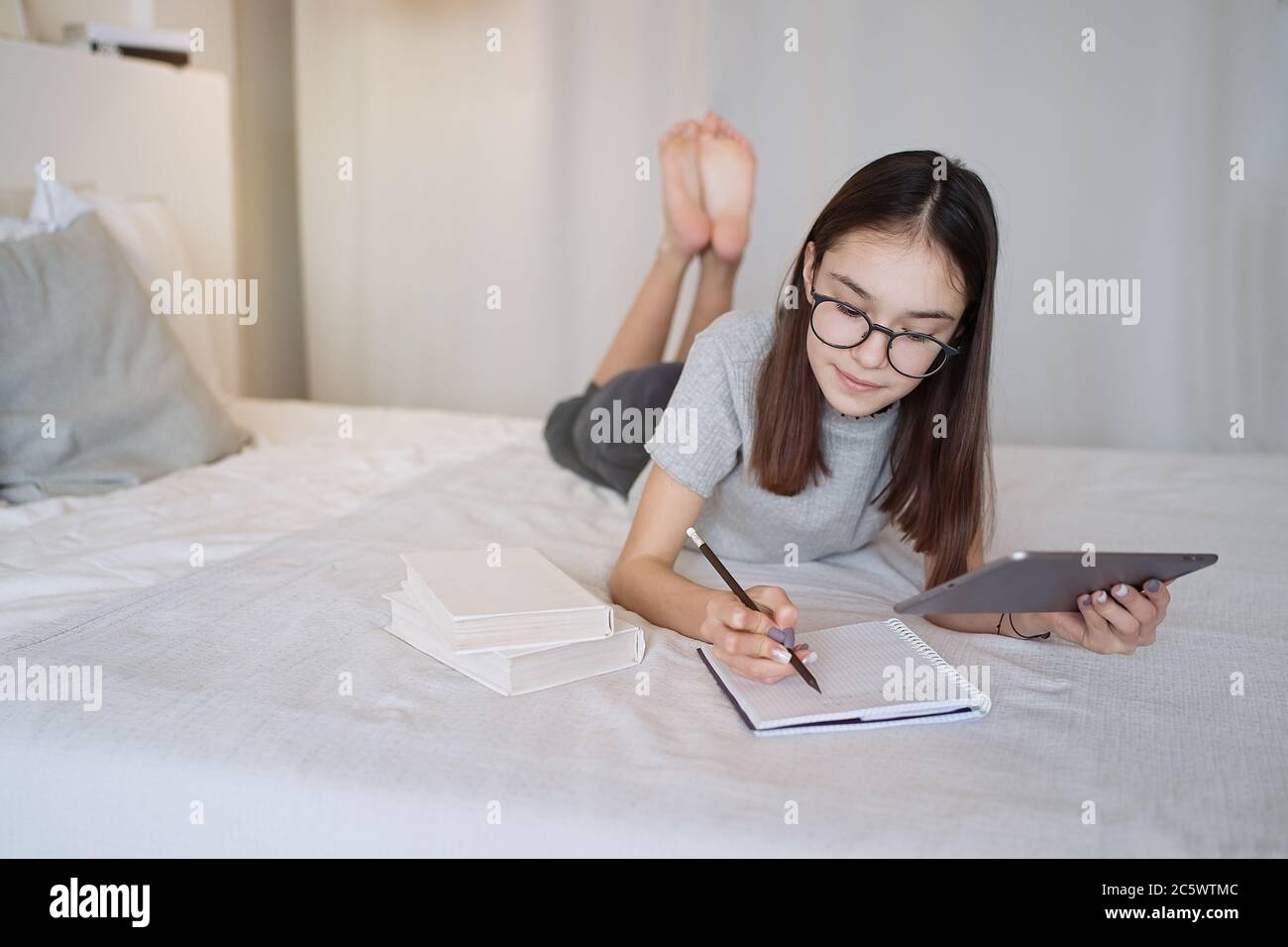 Teenage girl doing homework lying on bed at home. Pretty girl writing ...