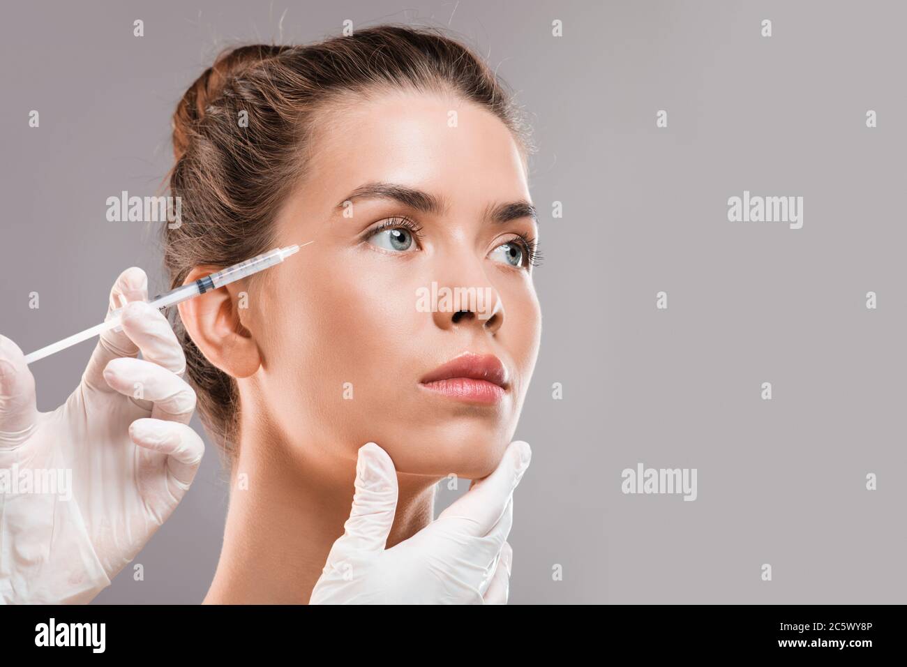 Young beautiful woman getting botox injection over grey background ...