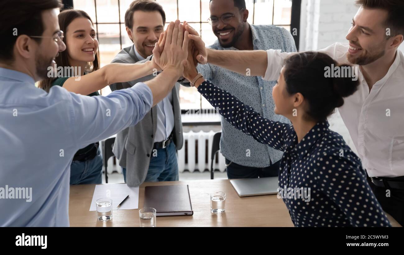 Excited multiethnic staff members giving high five sharing success ...